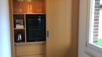 Quarto compacto com TV integrada, chaleira e uma prateleira pequena com copos.