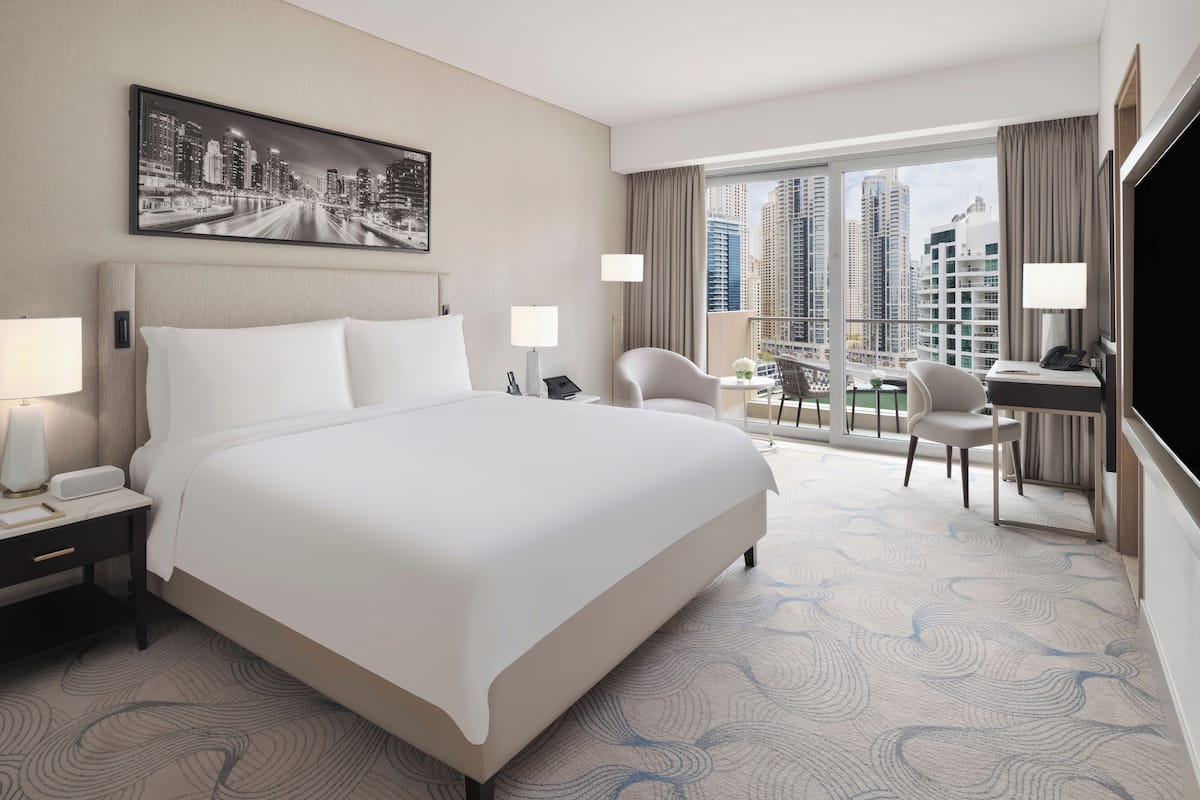 Quarto de hotel com uma cama grande, uma escrivaninha, duas cadeiras, uma televisão e vista para a cidade.