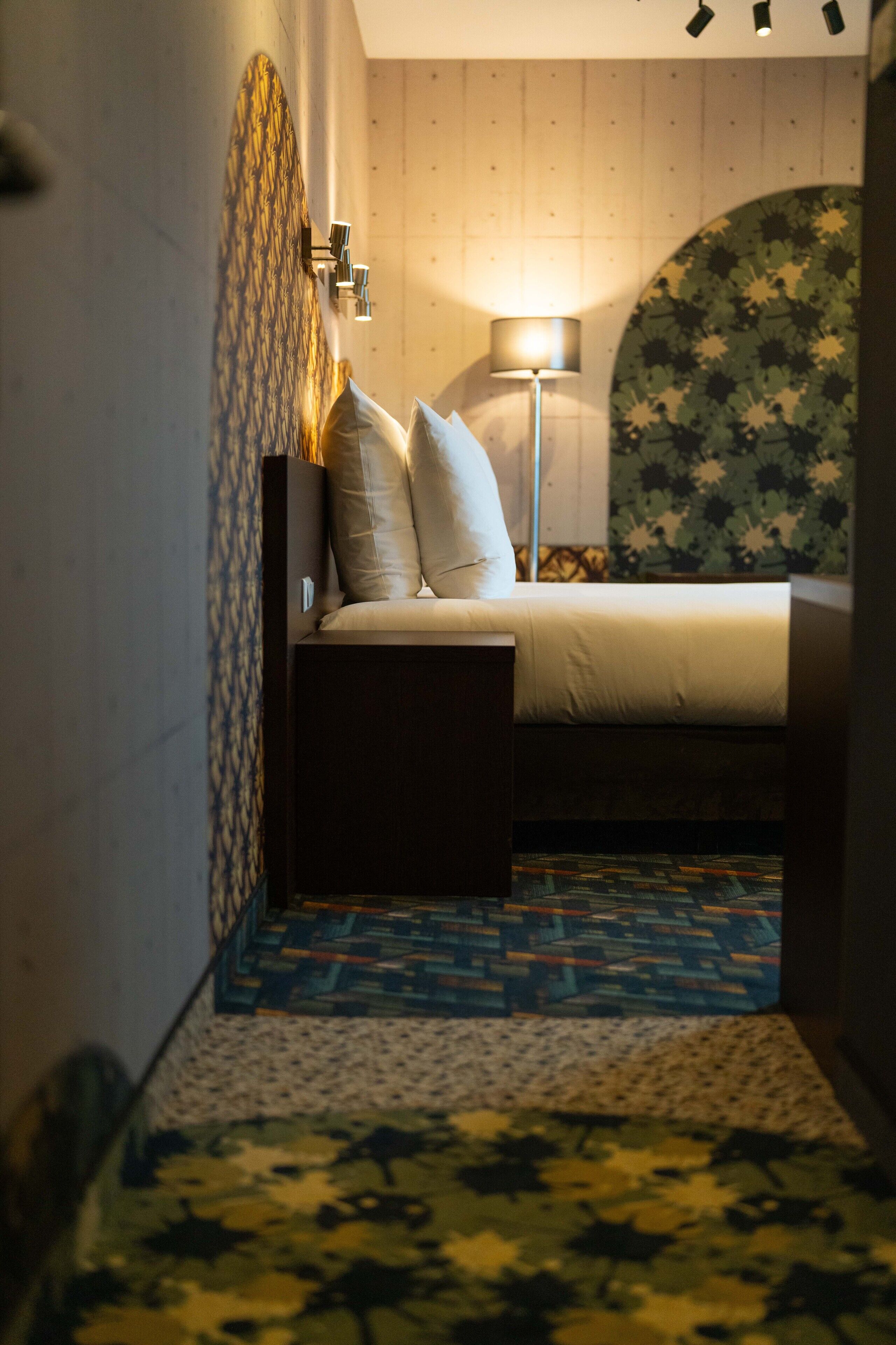 Quarto com cama, almofadas, abajur e paredes e chão estampados.