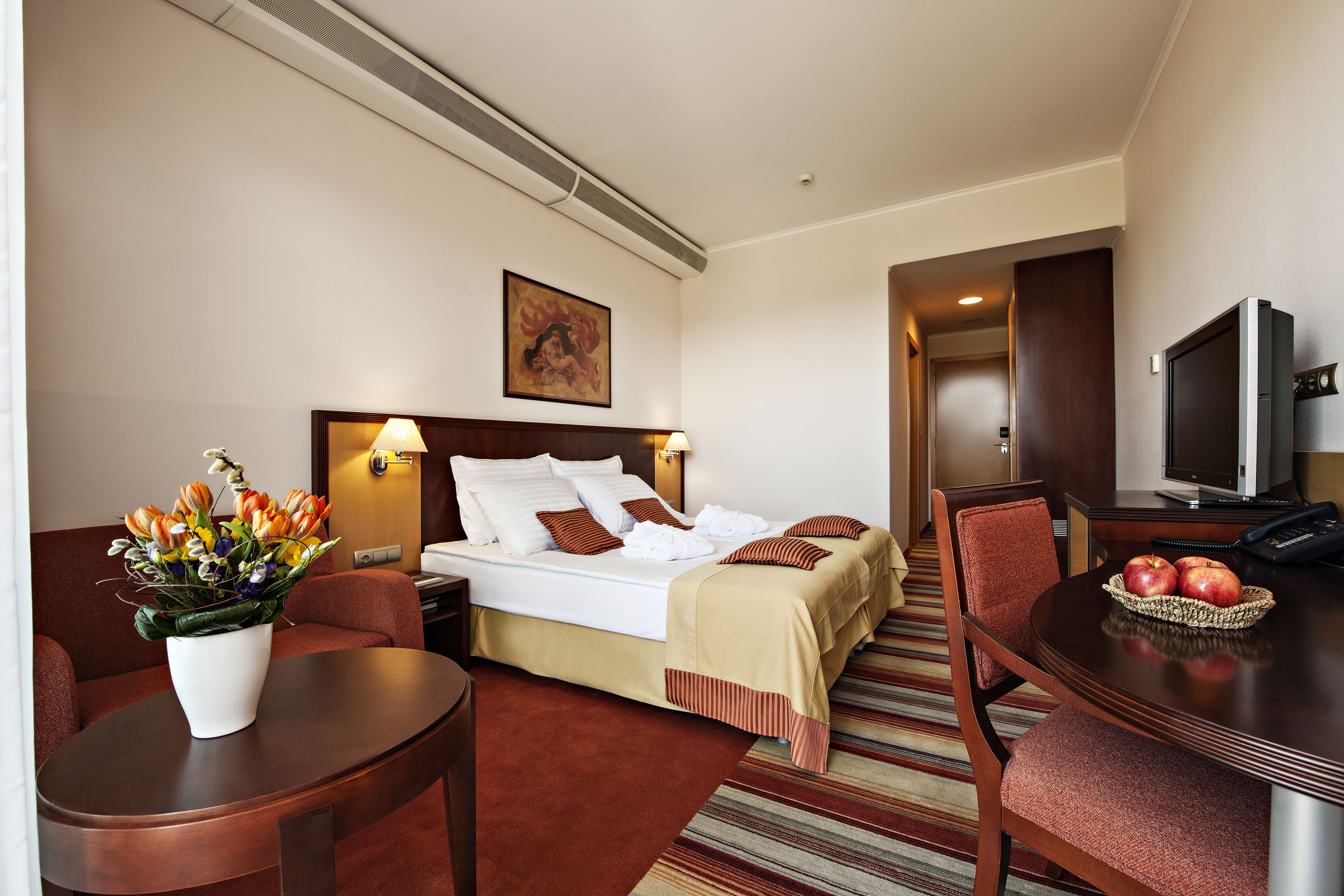 Quarto de hotel com cama, escrivaninha, cadeira, televisão e mesa de jantar com maçãs.