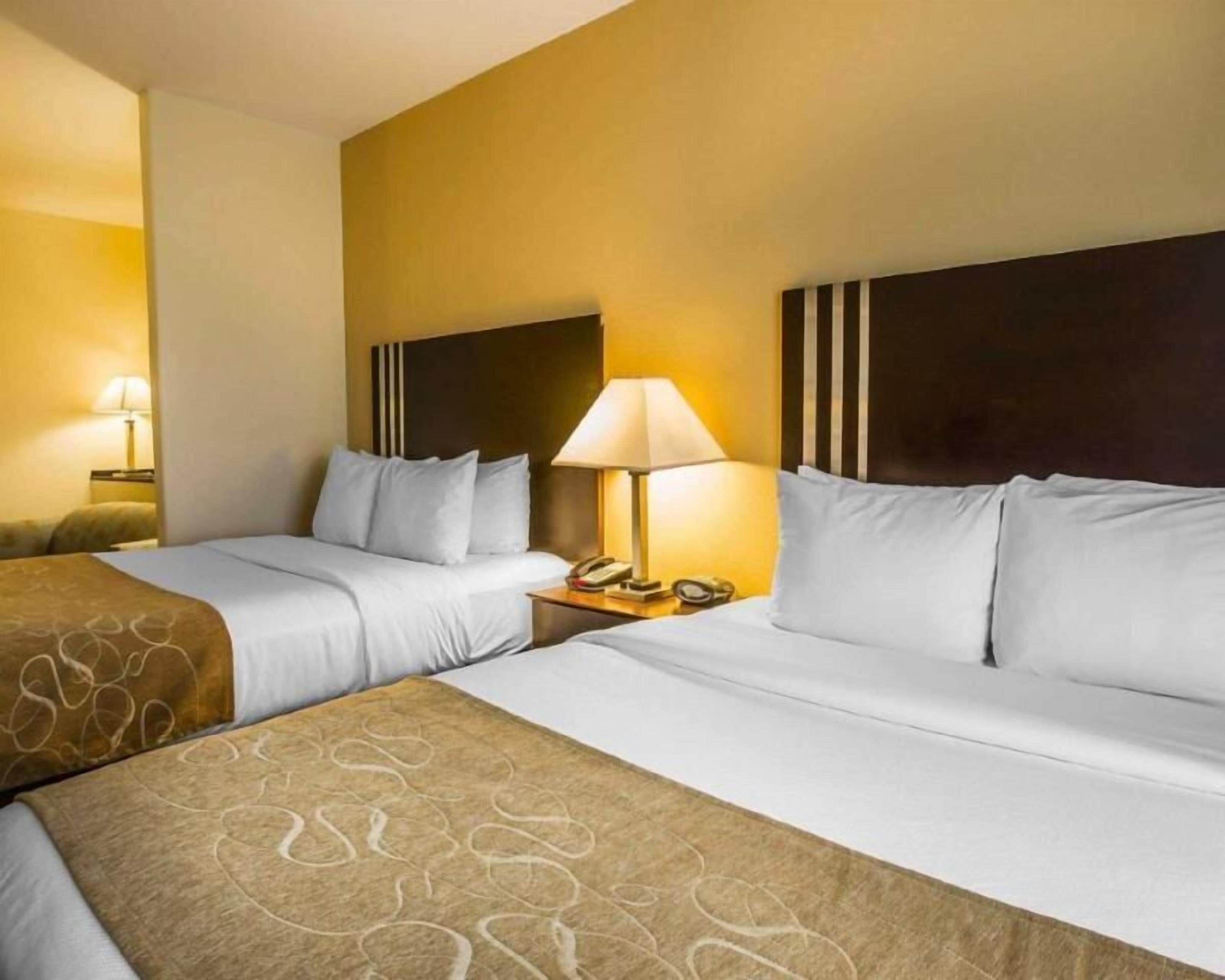 Quarto de hotel com duas camas, uma mesa de cabeceira com abajur e um telefone.