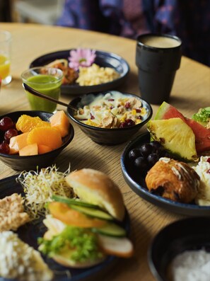 Um buffet de café da manhã com diversos pratos, incluindo frutas, pão e um smoothie verde.
