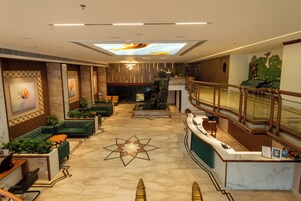 Um hall espaçoso com balcão de recepção, sofás verdes e um padrão decorativo em forma de estrela no chão.