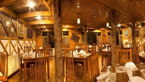 Interior rústico de madeira com várias mesas de jantar preparadas para hóspedes.