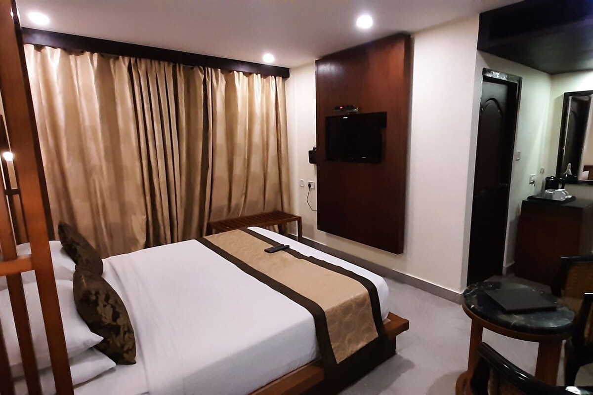 Quarto de hotel com cama, escrivaninha, cadeira, TV fixada na parede e espelho.