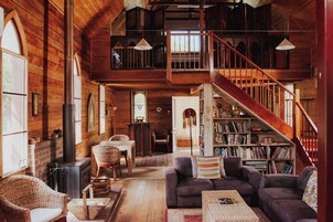 Um amplo loft com pé direito alto, vigas de madeira aparentes, escada e uma grande estante.