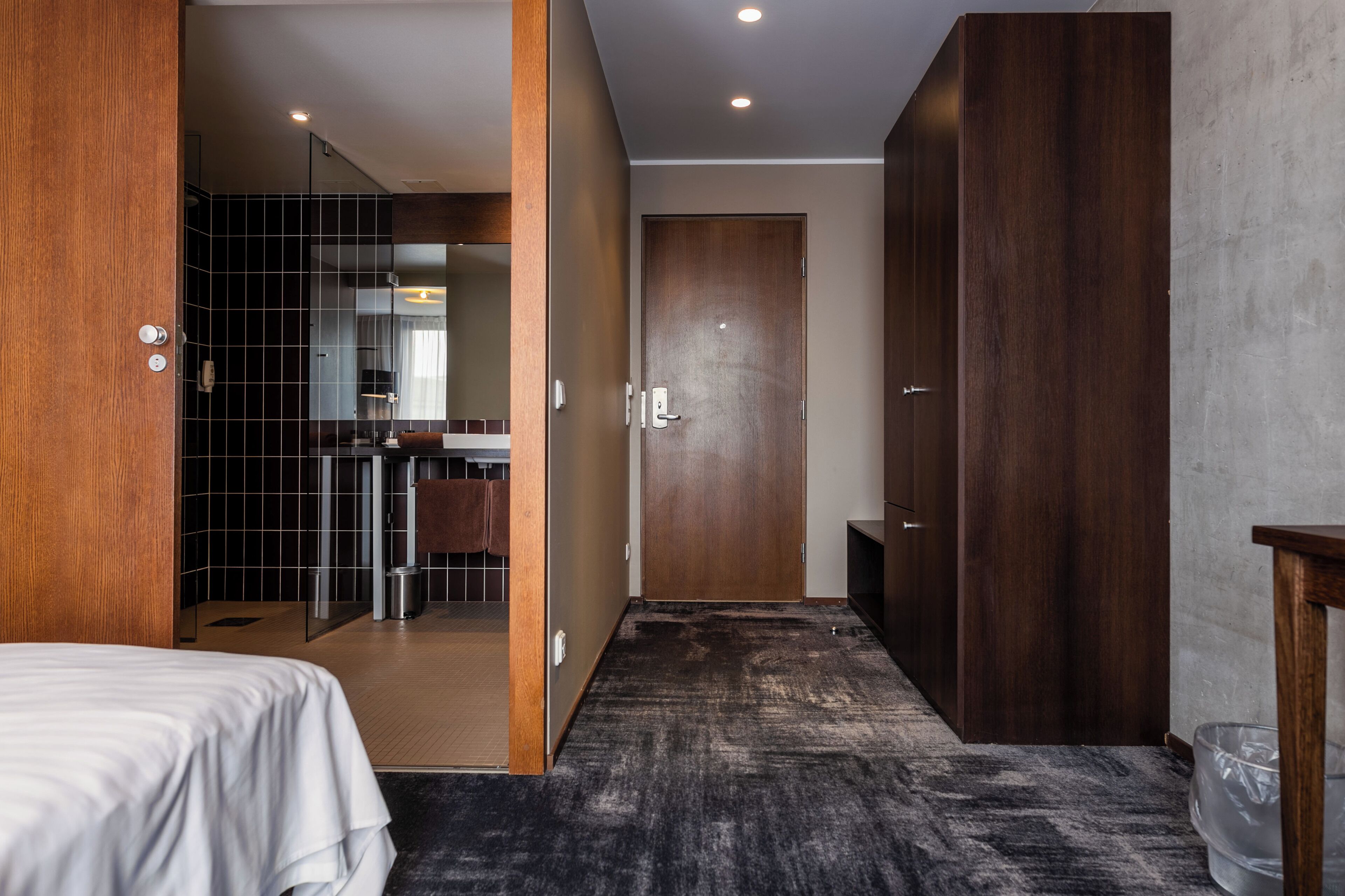 Quarto de hotel moderno com uma cama grande, um guarda-roupa de madeira, um banheiro pequeno e vista para a cidade.