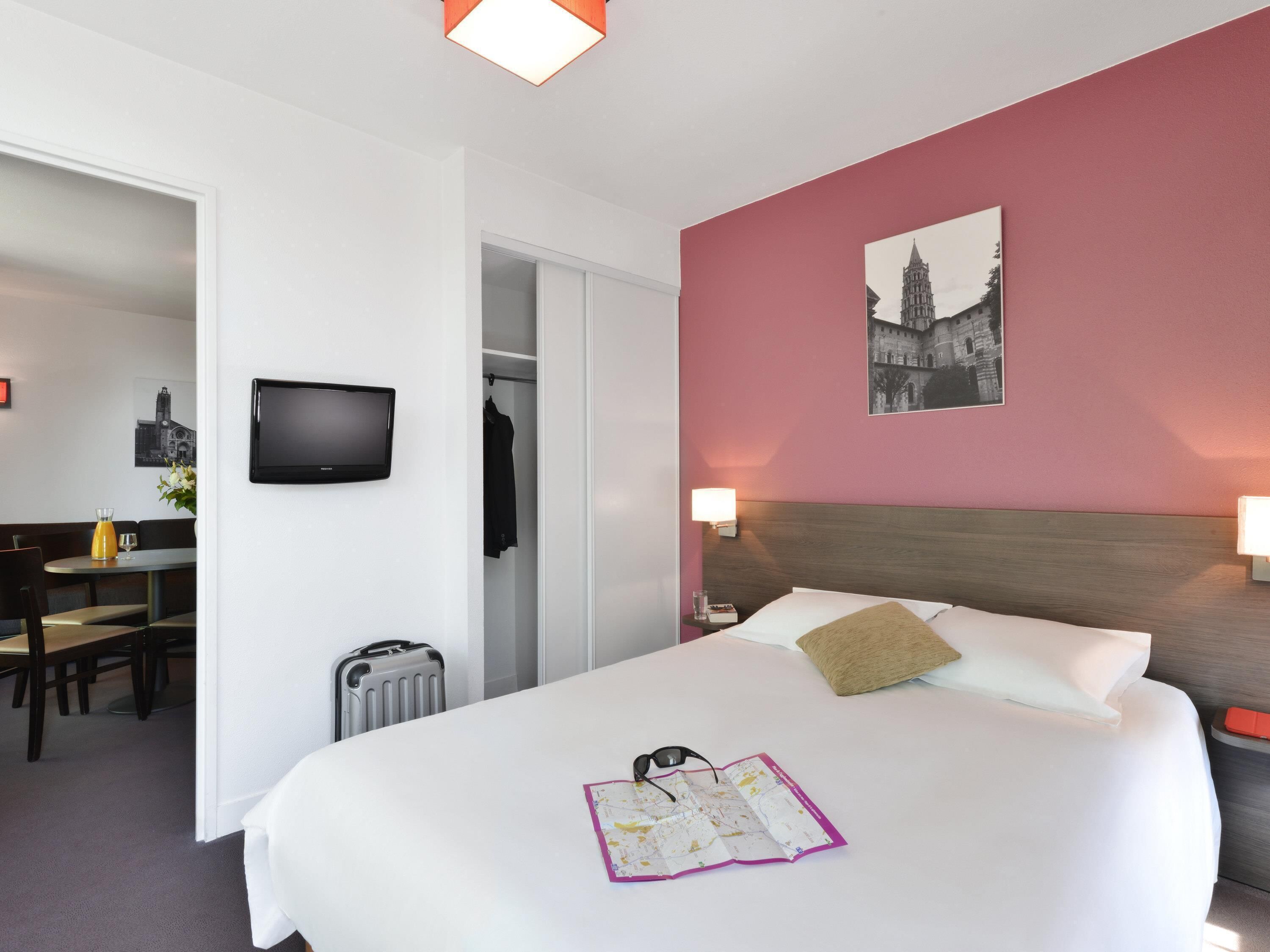 Quarto de hotel com uma cama, televisão, um mapa e um quadro na parede.