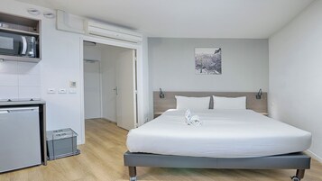 Quarto de hotel com cama, uma pequena cozinha e uma porta que dá para outro cômodo.