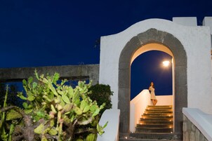 Escadaria que leva a uma varanda com uma pessoa no topo, sob um céu noturno.