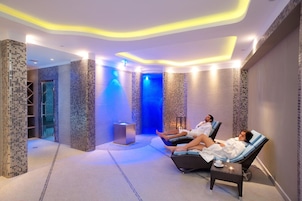Um quarto de spa com duas poltronas reclináveis, uma mesinha com uma vela e um aquecedor fixado na parede.