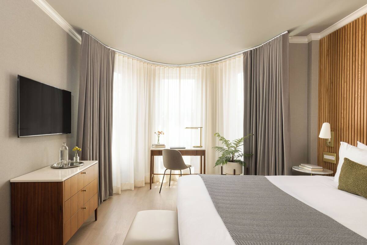 Quarto de hotel moderno com uma cama grande, uma escrivaninha, uma televisão e vista para o exterior.