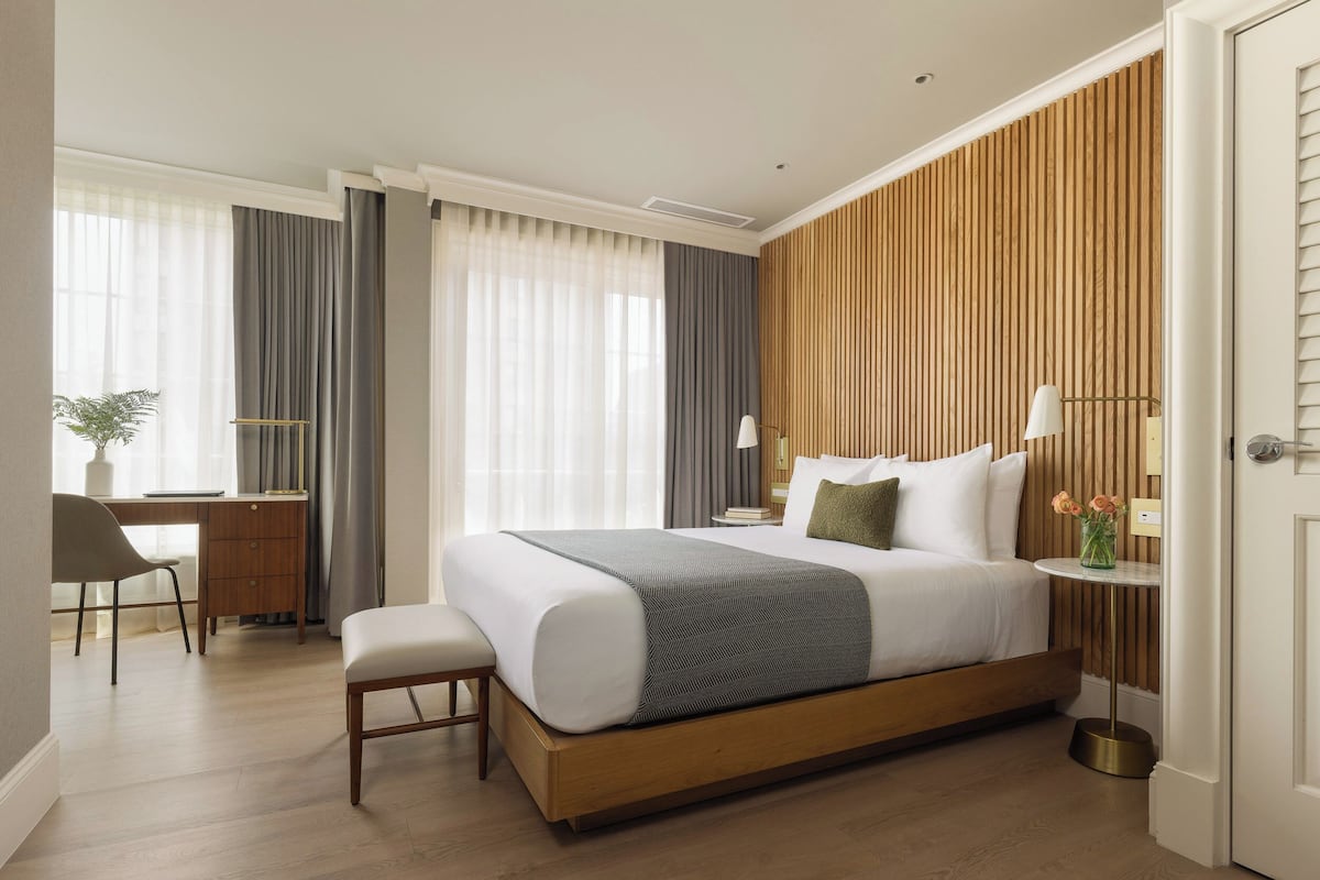Quarto de hotel moderno com uma cama grande, uma escrivaninha e uma pequena mesa com flores.