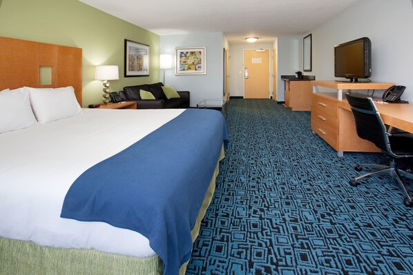 Quarto de hotel com uma cama grande, uma escrivaninha com um computador, uma cadeira, um abajur e uma porta que dá para o banheiro.