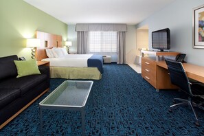 Quarto de hotel com cama, secretária com computador, sofá e mesa de centro.