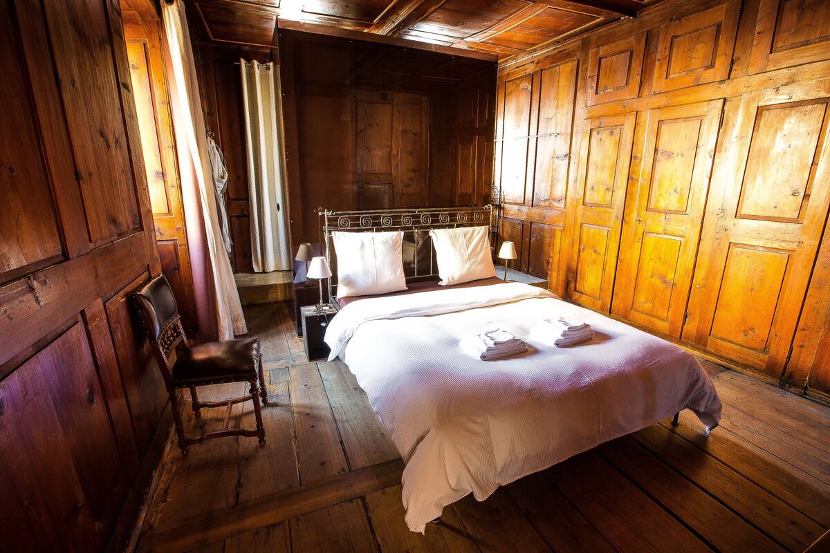Quarto de madeira com uma cama, uma cadeira e uma mesa de cabeceira.