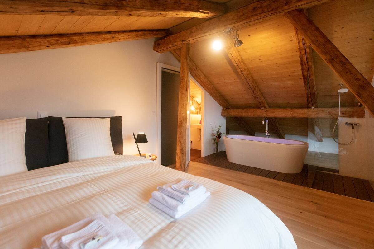 Quarto com uma cama grande, teto de madeira, banheiro com banheira e box de vidro.