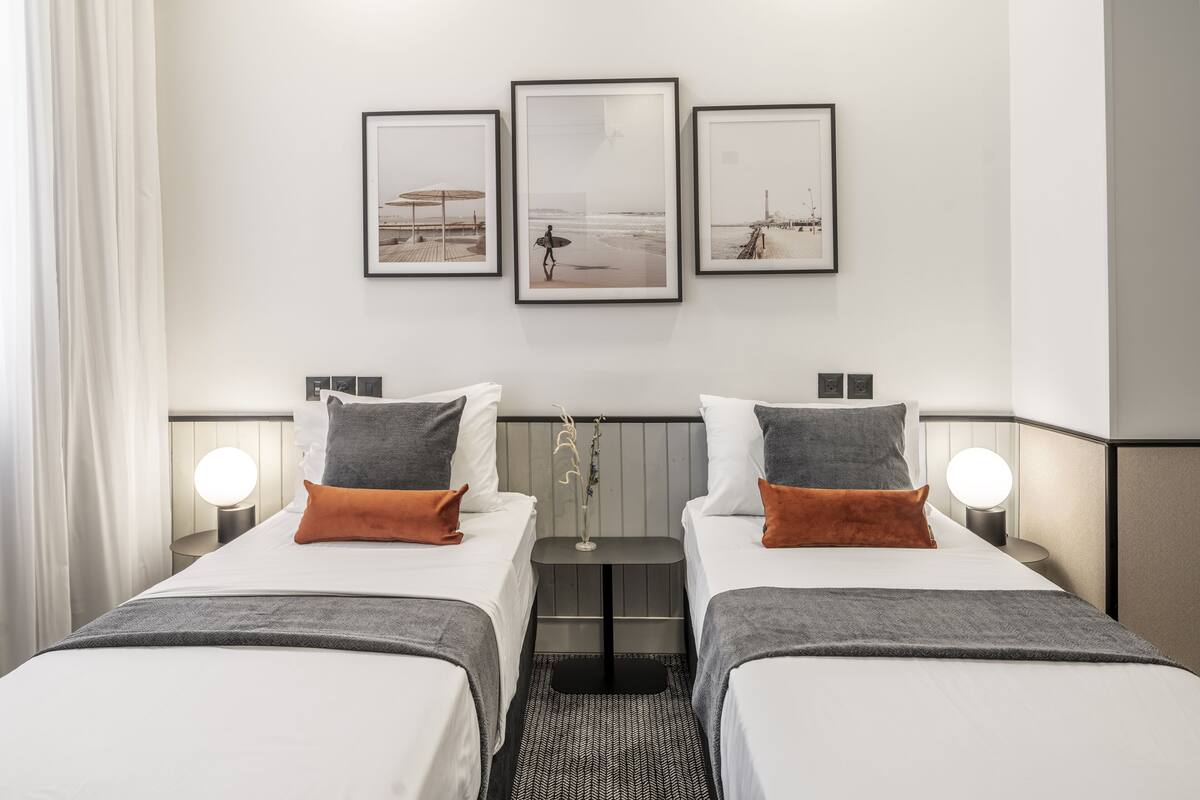 Quarto de hotel com duas camas, uma mesa pequena e três quadros na parede.