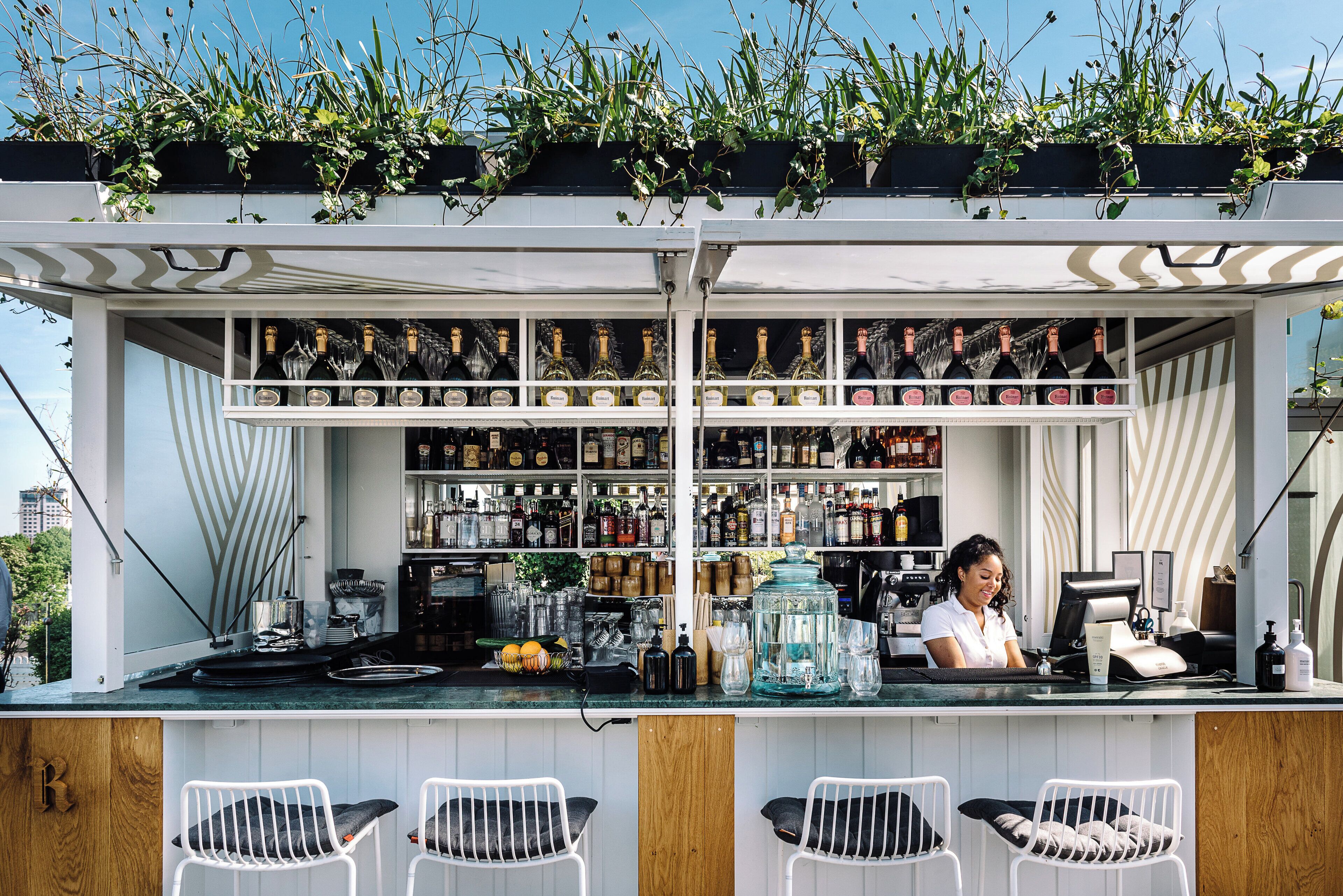 Uma área de bar com prateleiras de garrafas, um balcão e duas cadeiras brancas.