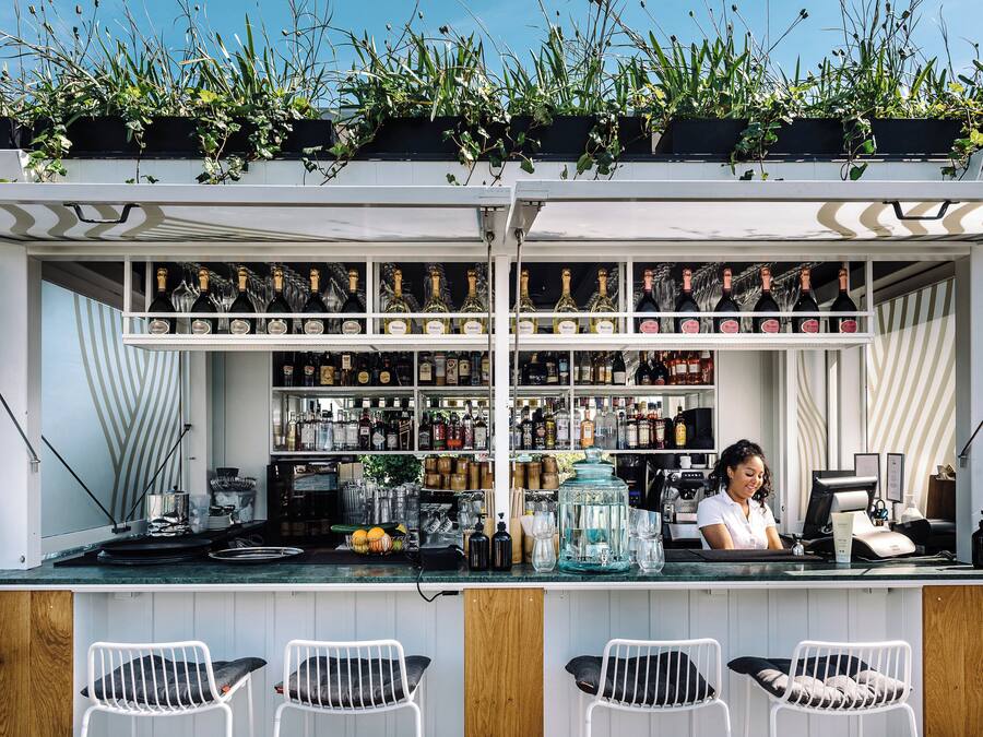 Uma área de bar com prateleiras de garrafas, um balcão e duas cadeiras brancas.