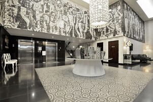 Um lobby moderno com uma mesa central, elevadores e um piso estampado.