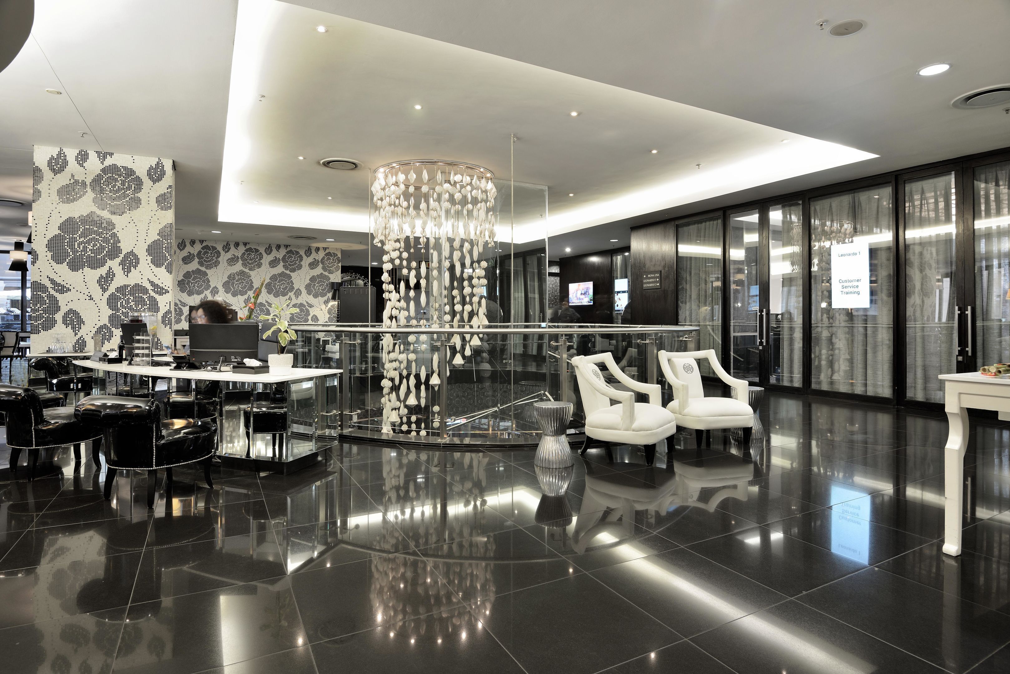 Um saguão de hotel moderno com um lustre central, balcão de recepção e áreas de estar.
