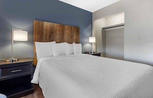 Quarto de hotel com cama, mesas de cabeceira, arara para roupas e uma luminária.