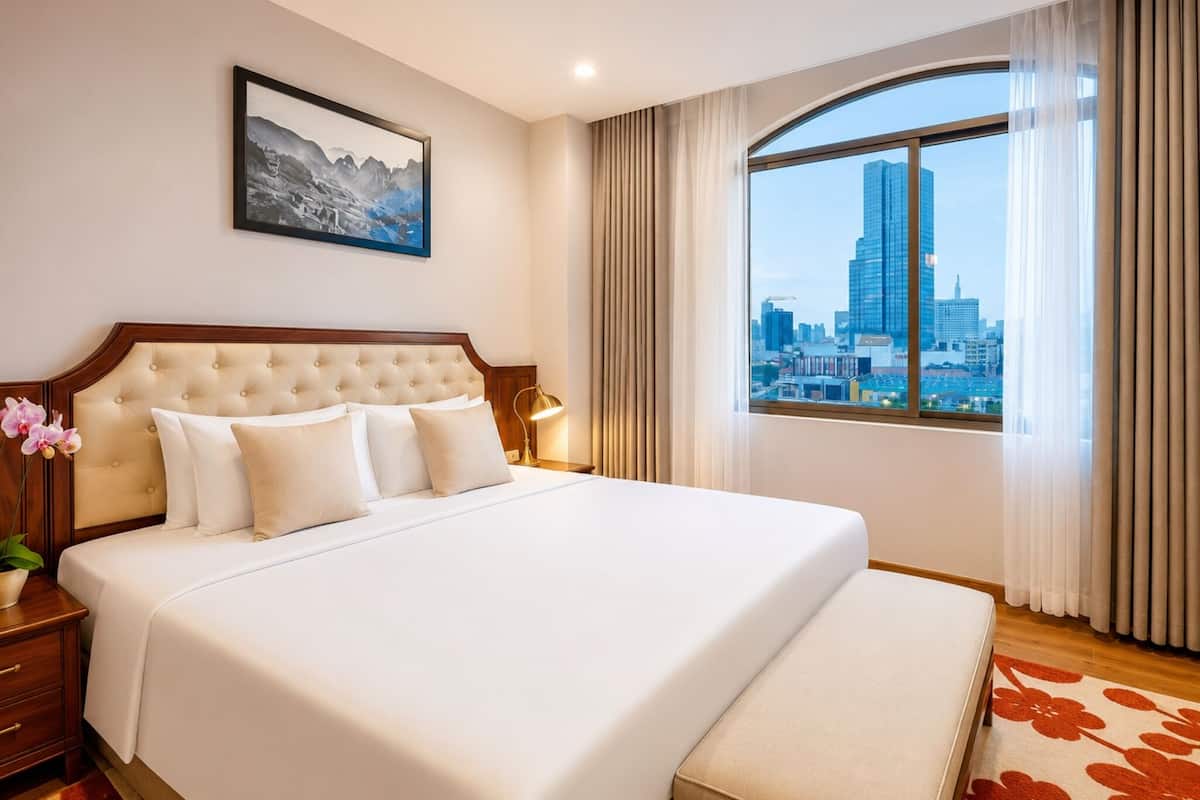 Quarto de hotel com uma cama grande, vista da cidade, um quadro na parede e mesa de cabeceira com abajur.