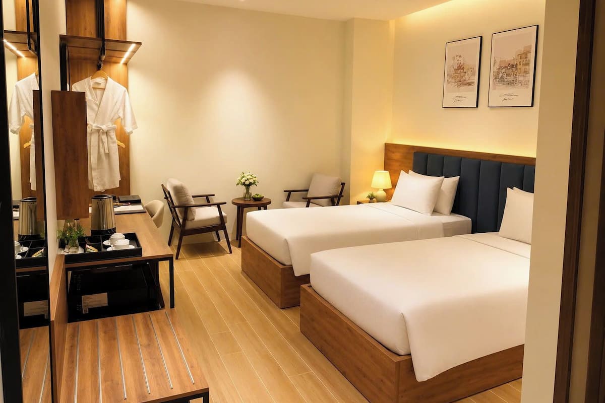 Quarto de hotel com duas camas, uma escrivaninha, cadeiras, um espelho e obras de arte na parede.