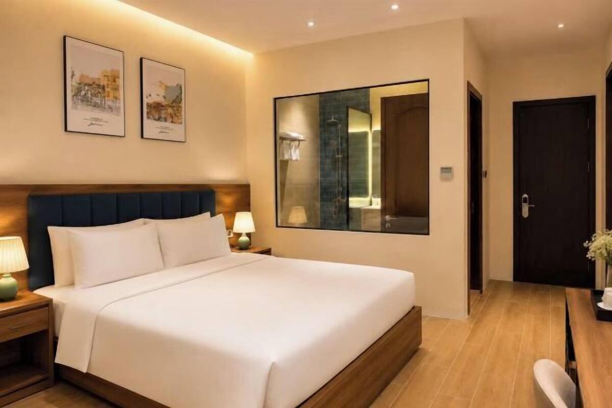 Quarto de hotel com uma cama grande, mesa de cabeceira com abajur, espelho e duas imagens emolduradas na parede.