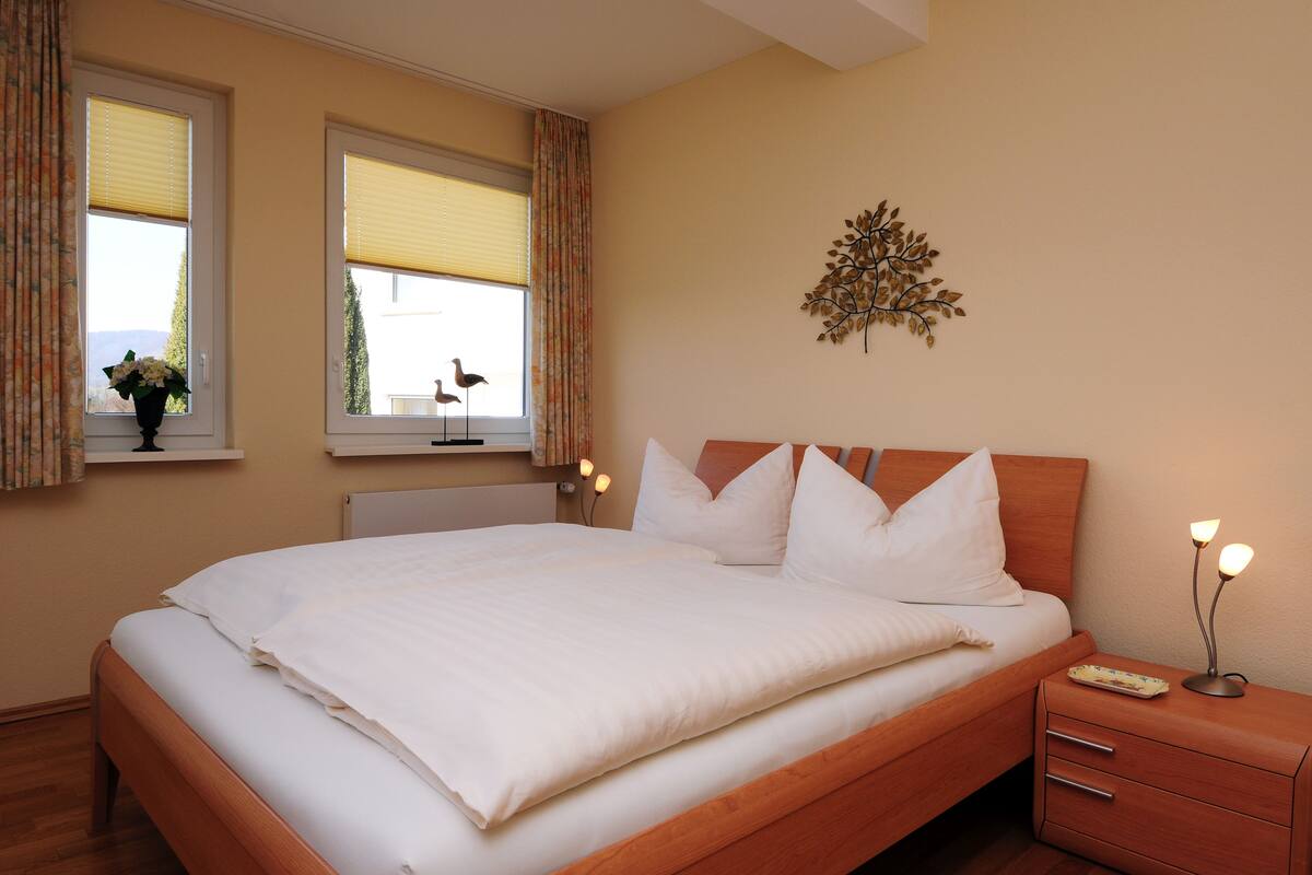 Uma cama bem arrumada com lençóis brancos, uma cabeceira de madeira e uma mesa de cabeceira com abajur.
