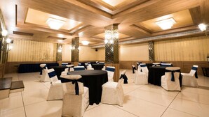 Uma sala de banquetes com mesas e cadeiras redondas, vigas de madeira no teto e iluminação embutida.