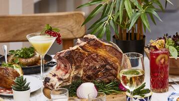 Uma mesa posta com um pernil assado, acompanhamentos diversos e bebidas.