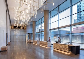 Um hall amplo com design moderno, com um balcão de recepção, grandes janelas e teto alto com luminárias pendentes.