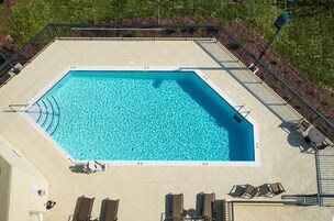Piscina retangular com um deck ladrilhado ao redor, equipada com espreguiçadeiras e uma área de estar coberta.