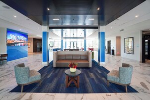 Um hall com carpete azul, um sofá, duas poltronas e uma mesa com um vaso de flores.