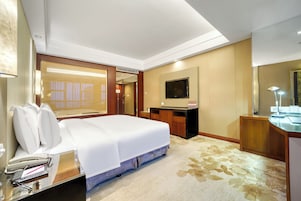 Quarto de hotel com uma cama grande, uma escrivaninha, uma televisão e um espelho.