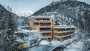 Um edifício moderno de vários andares com fachada de madeira, cercado por montanhas e árvores cobertas de neve.