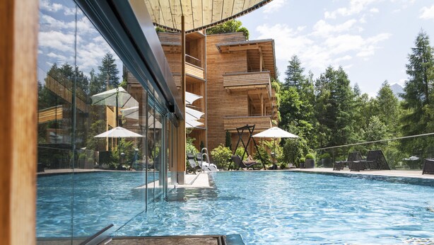 Um hotel moderno com piscina, área de estar externa e vista para a floresta ao redor.