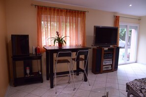 Uma sala de estar com televisão, planta, duas cadeiras e uma pequena mesa.