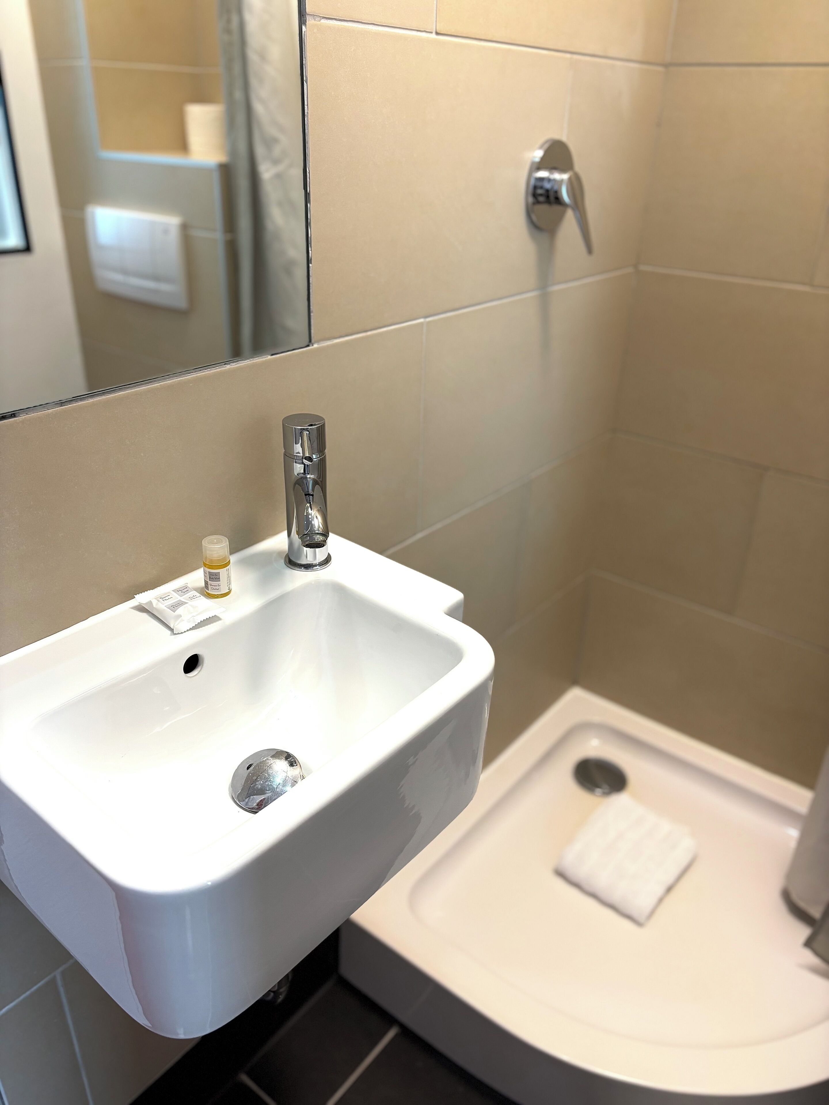 Casa de banho com lavatório branco, espelho e chuveiro.