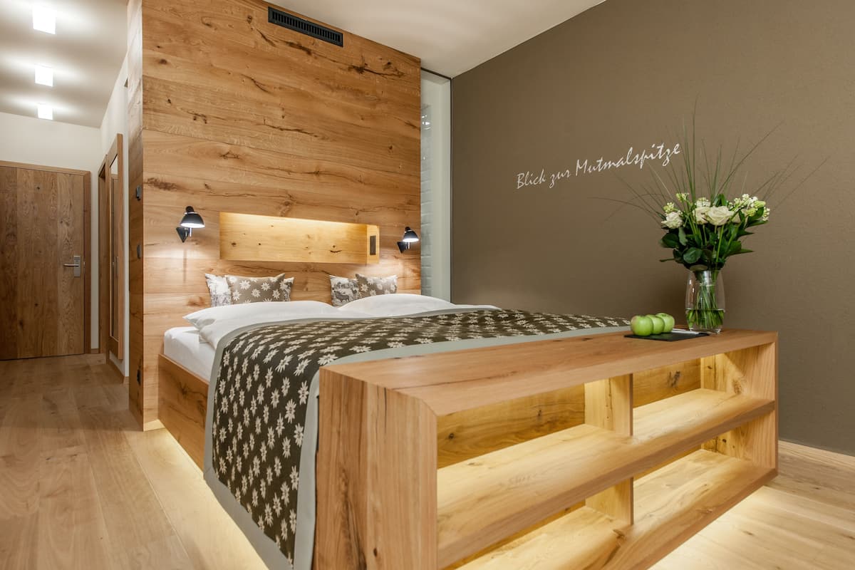 Quarto com cabeceira de madeira, mesa de cabeceira com um vaso de flores e parede com uma placa de texto.