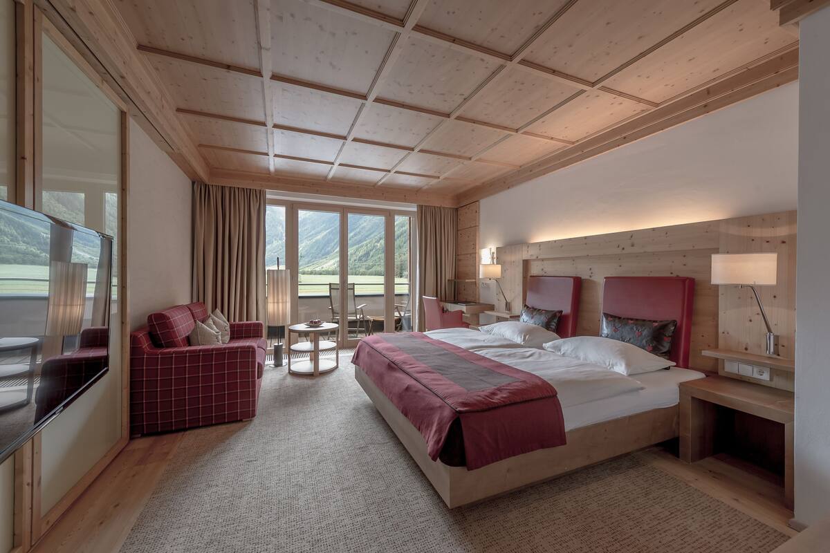 Quarto de hotel com uma cama grande, um sofá, uma escrivaninha e uma janela com vista para as montanhas.