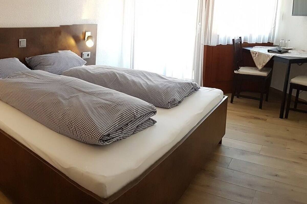 Uma cama de casal com cabeceira, luminárias laterais e uma escrivaninha com cadeira.