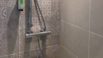 Um chuveiro com um chuveiro manual e uma mangueira, fixados numa parede com azulejos estampados.