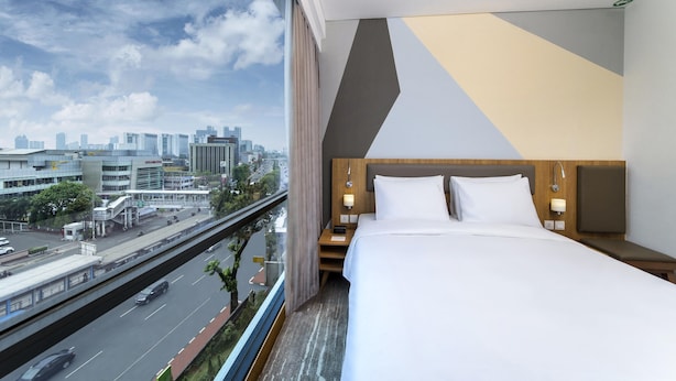 Quarto de hotel com uma cama grande, mesas de cabeceira e vista para a cidade através de uma janela ampla.