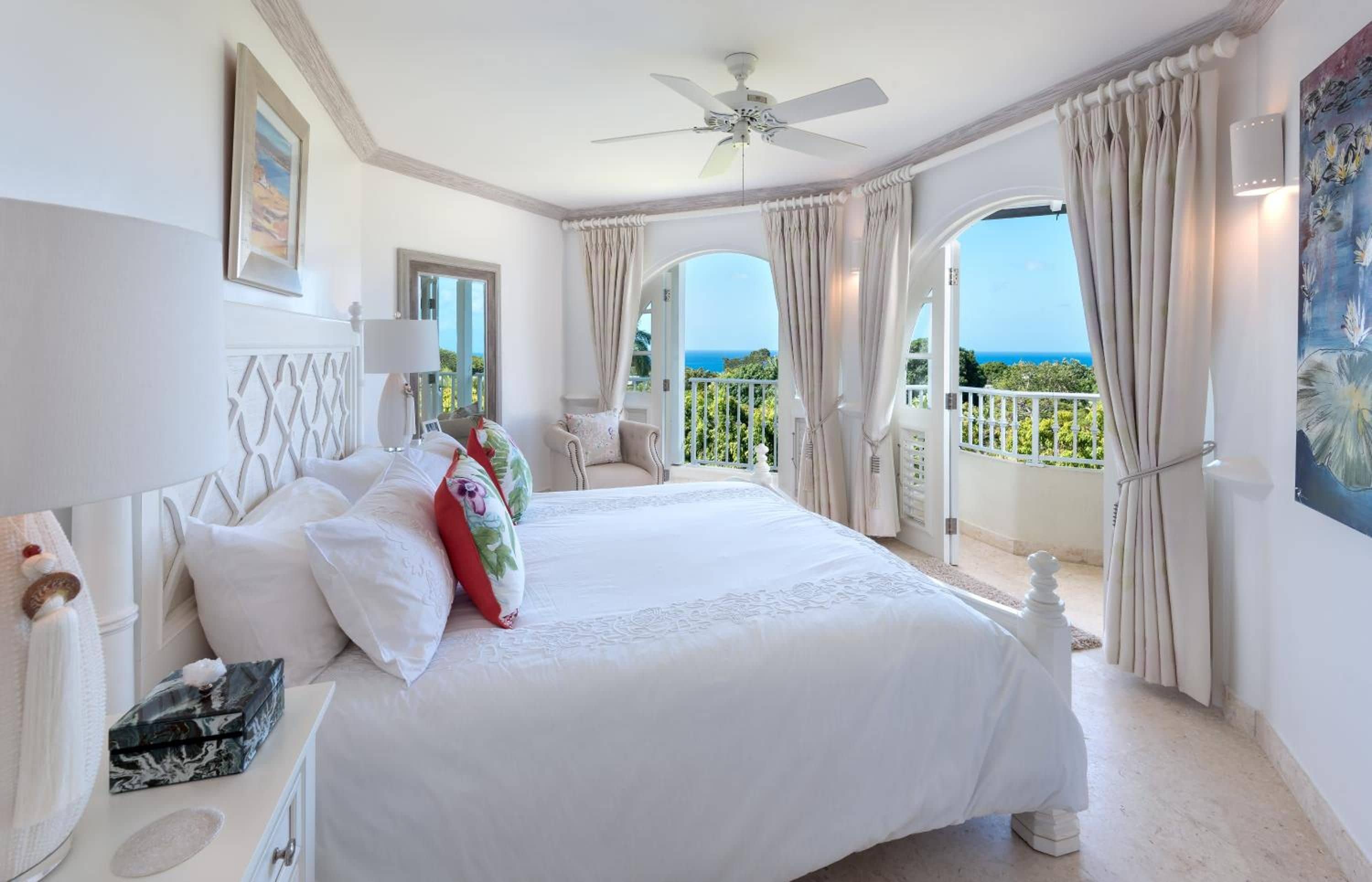 Quarto com cama grande, ventilador de teto e vista para o oceano pelas portas da varanda.