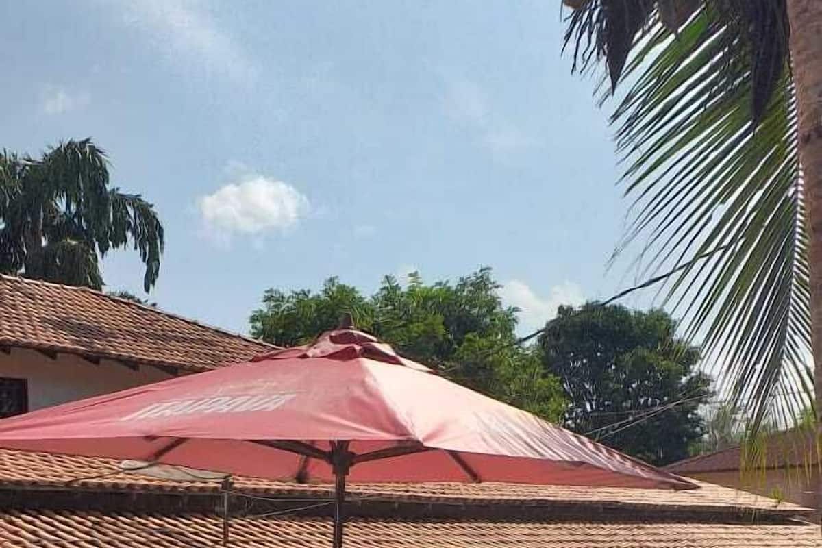 Uma área de pátio com um guarda-sol vermelho, cadeiras de madeira e uma pequena mesa.