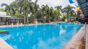 Piscina com deck revestido, cercada por palmeiras e estruturas cobertas.
