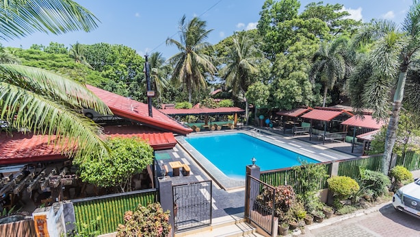 Piscina cercada por área com assentos externos e um edifício com telhado vermelho.